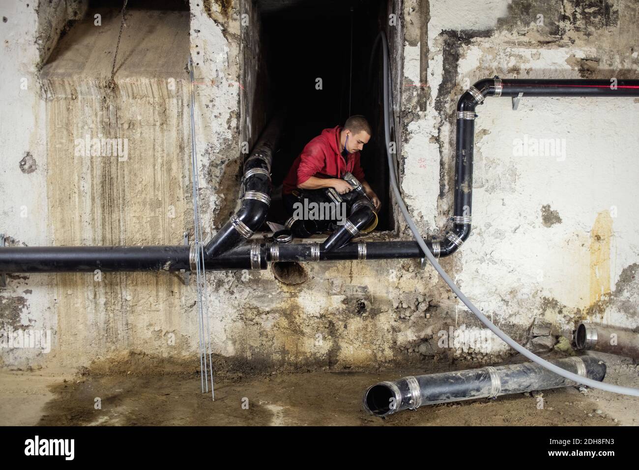 Male plumber connecting pipes amidst walls in basement Stock Photo - Alamy