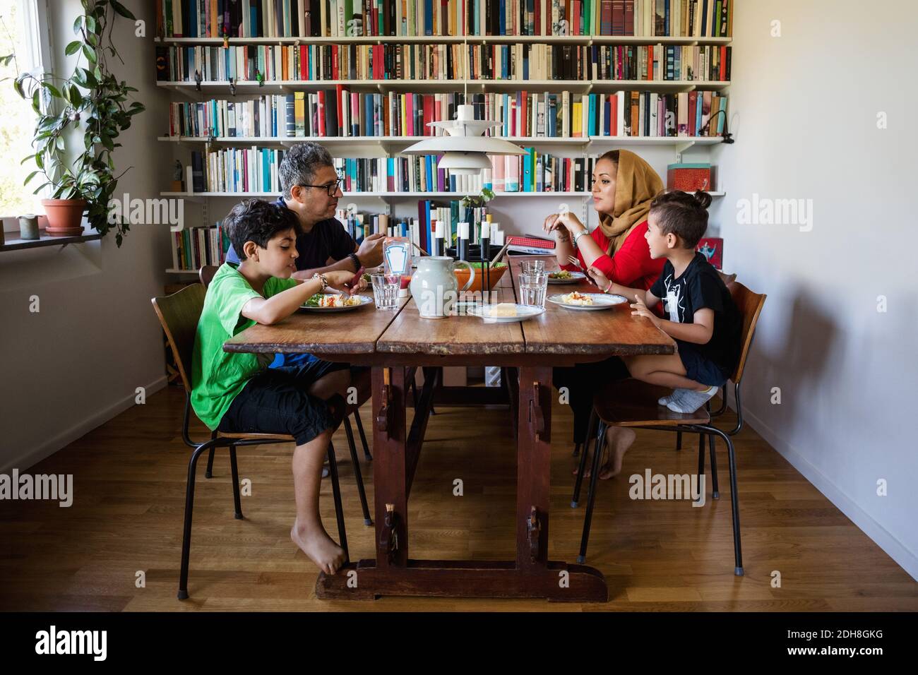 Family having meal at table by bookshelf Stock Photo - Alamy