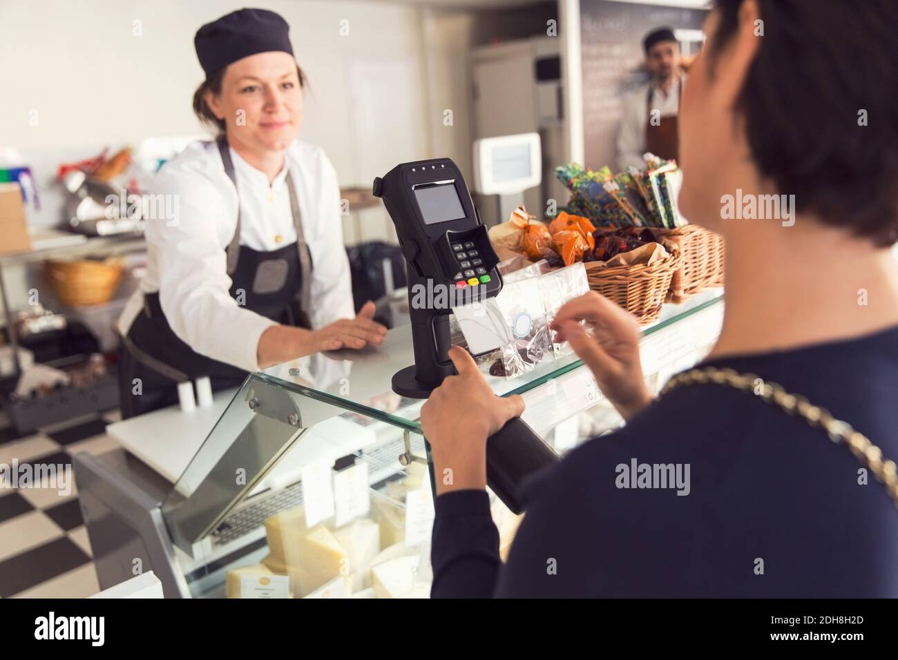 Saleswoman looking at female customer entering pin in credit card ...