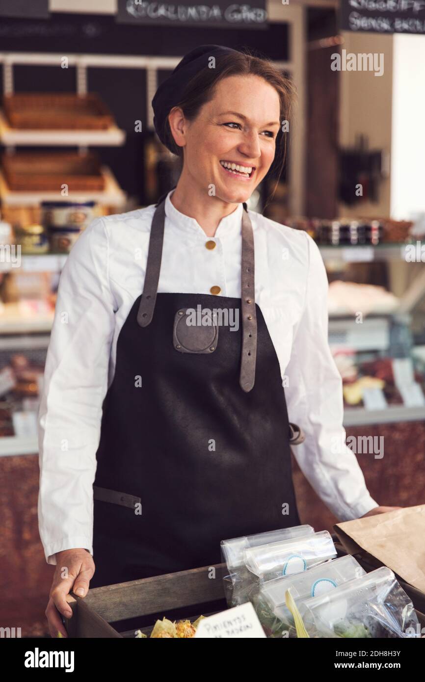 Happy female owner looking away while standing in grocery store Stock ...