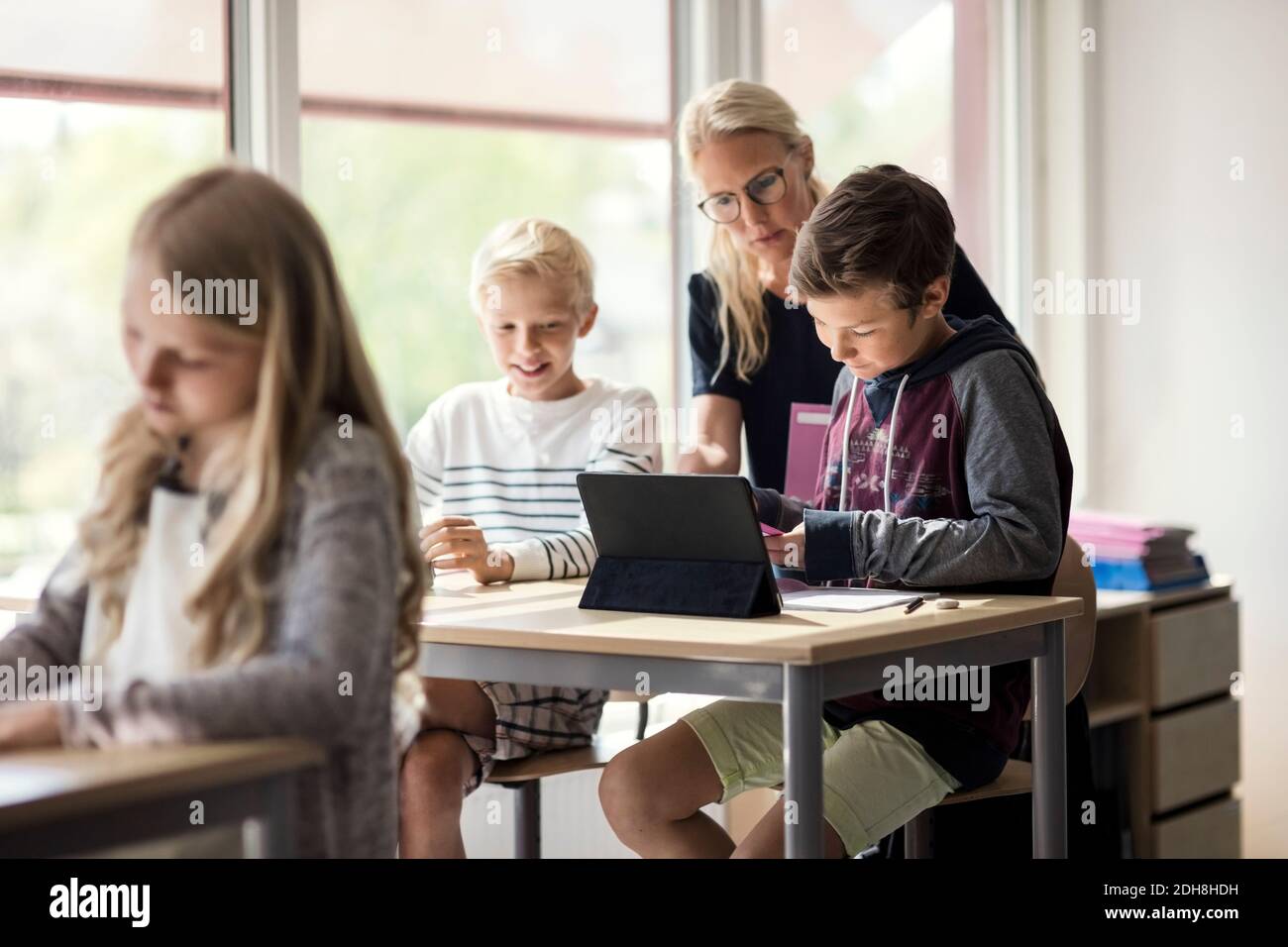 Teacher assisting children in e-learning from digital tablet Stock ...
