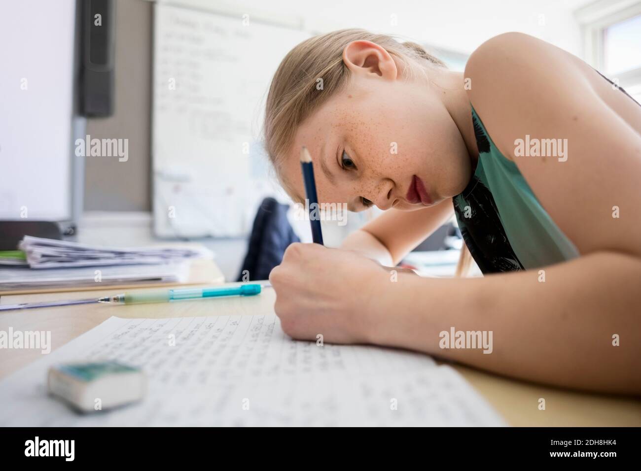 Side view of girl writing in book at classroom Stock Photo - Alamy