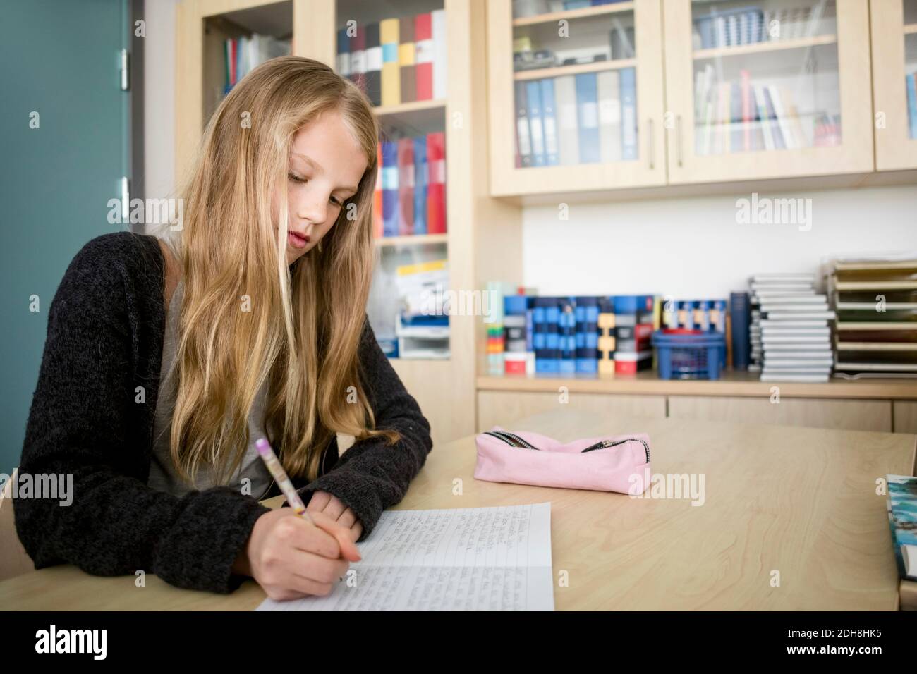 Girl writing in book on desk at classroom Stock Photo - Alamy