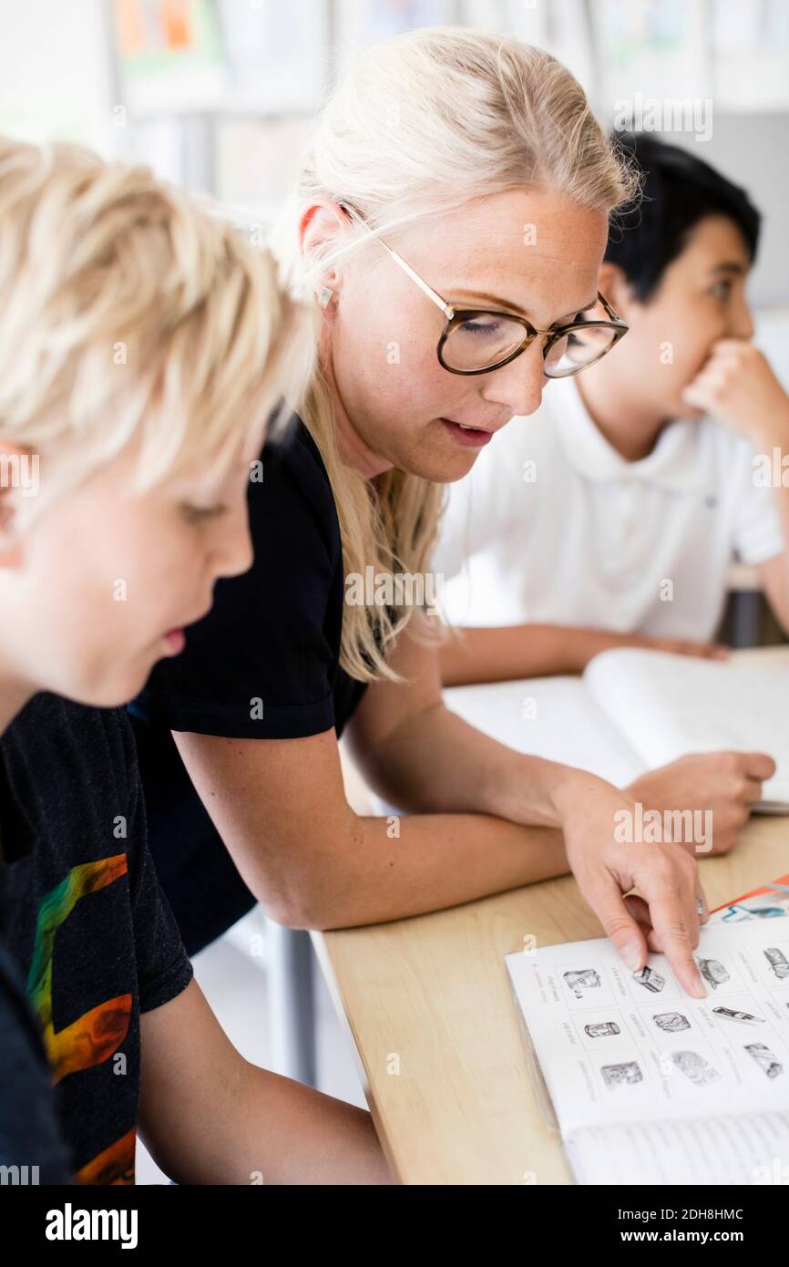 Teacher explaining from book to student in classroom Stock Photo - Alamy