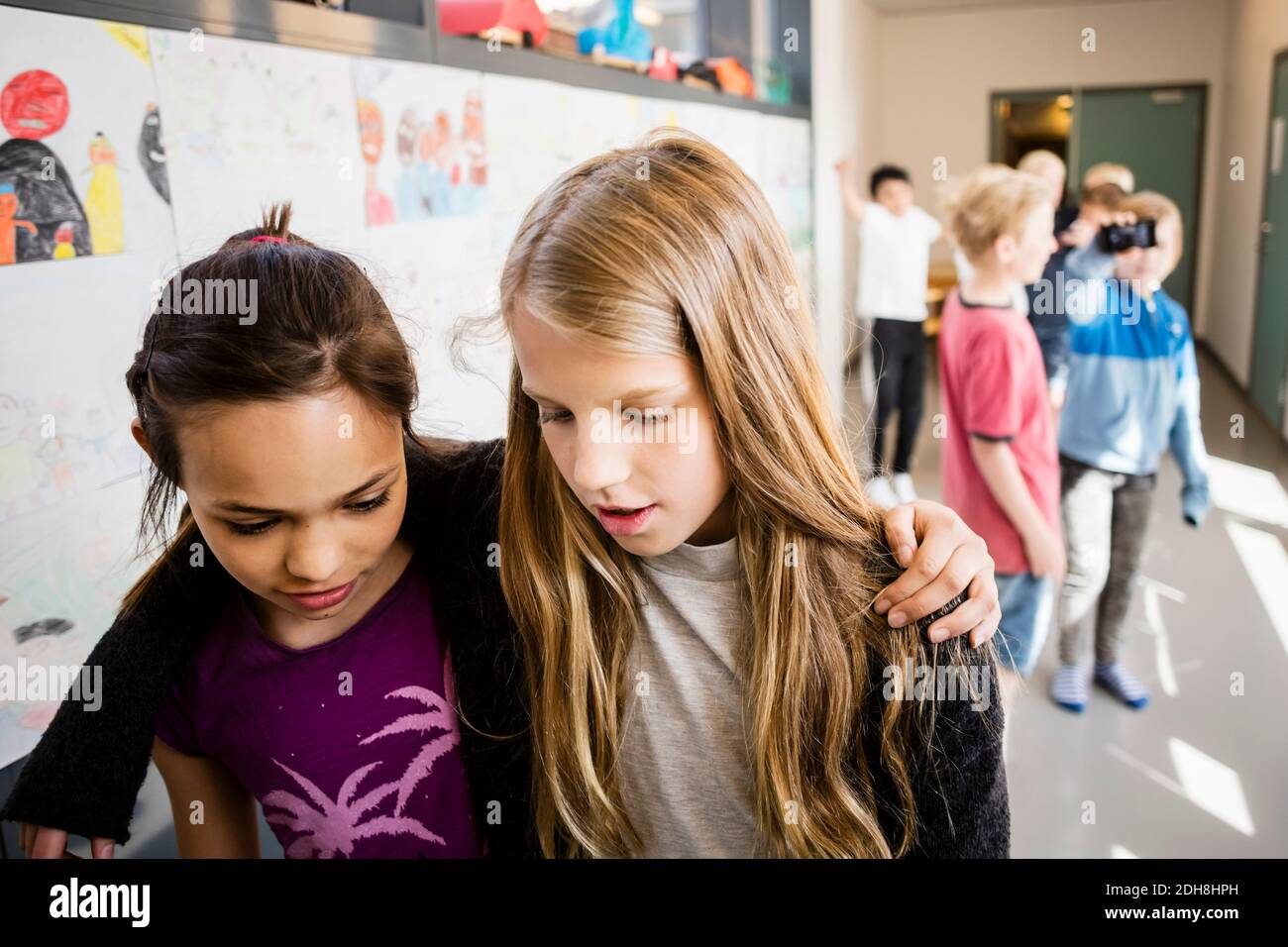 Girls walking with arms around against friends in corridor at school ...