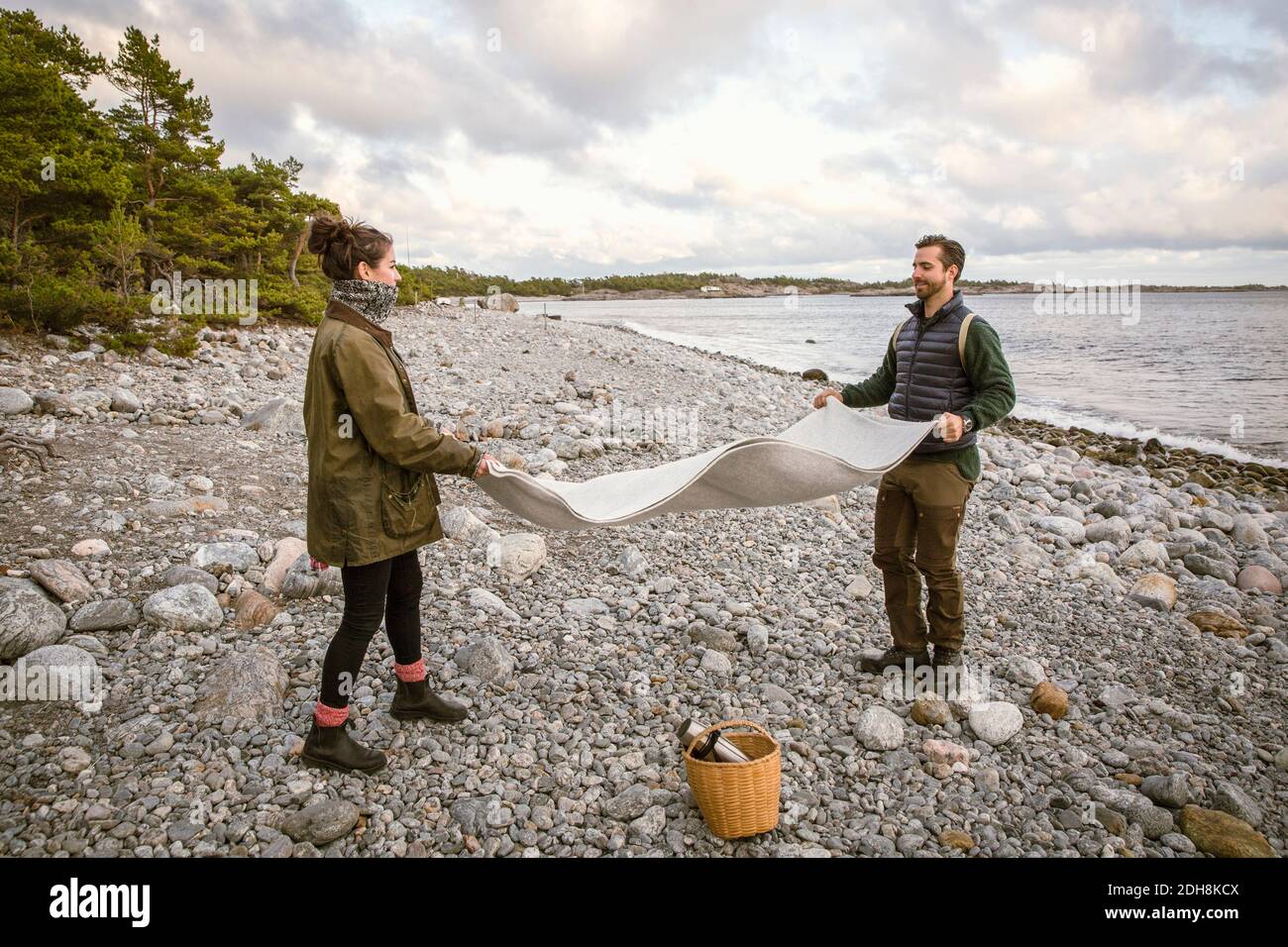 Couple placing blanket on rocky shore at beach during sunset Stock ...