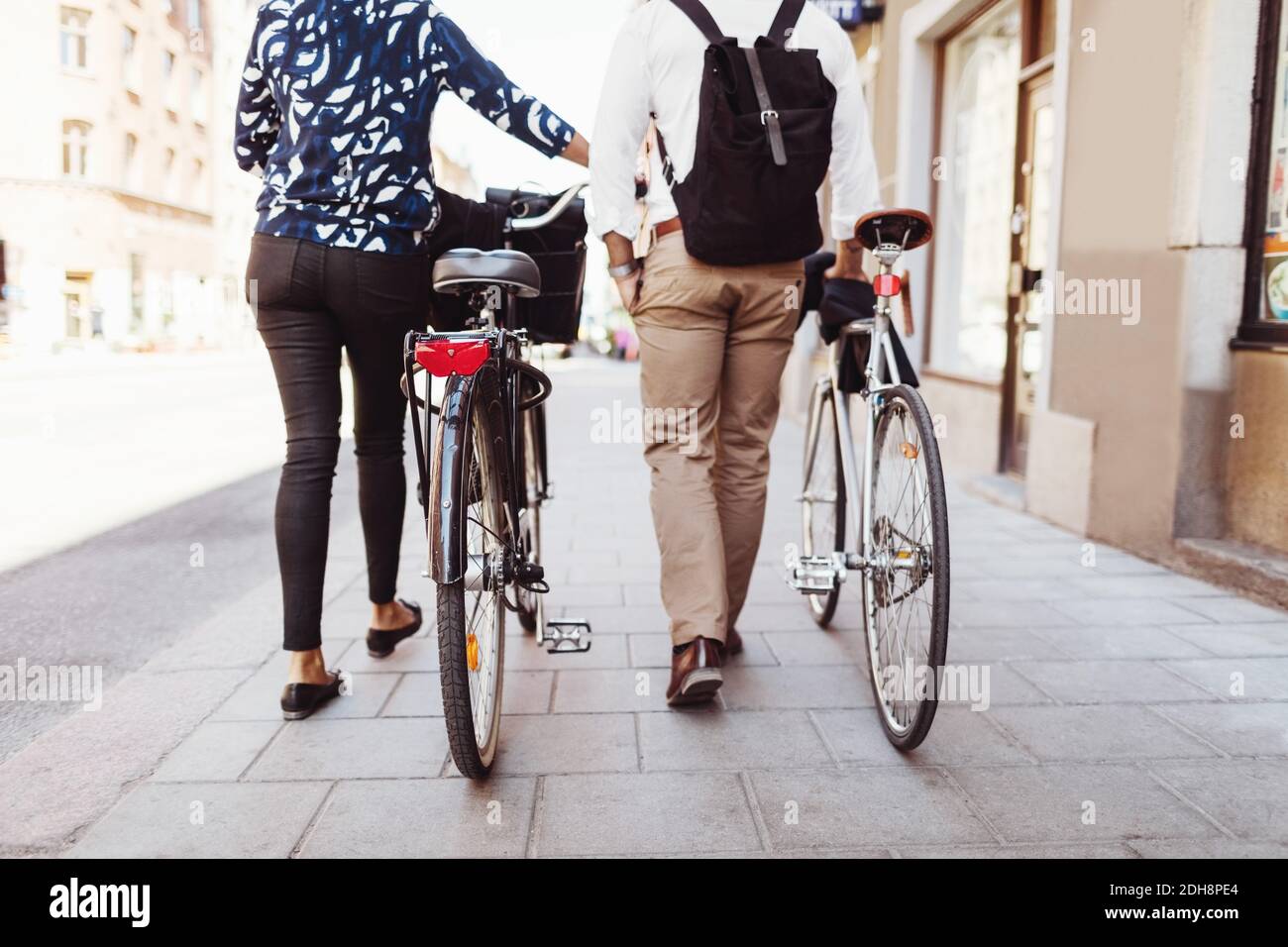Low section rear view of business colleagues walking with bicycles on ...