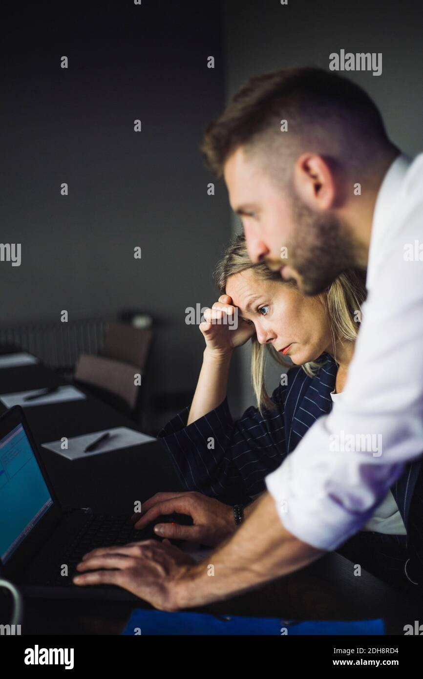 IT professional working on laptop by worried colleague at workplace ...