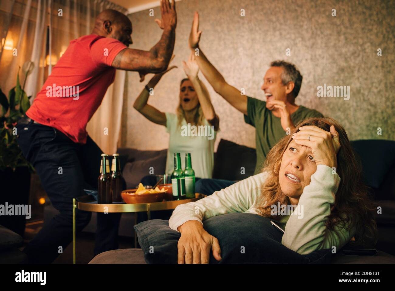 Disappointed woman sitting on sofa while friends cheering in background ...