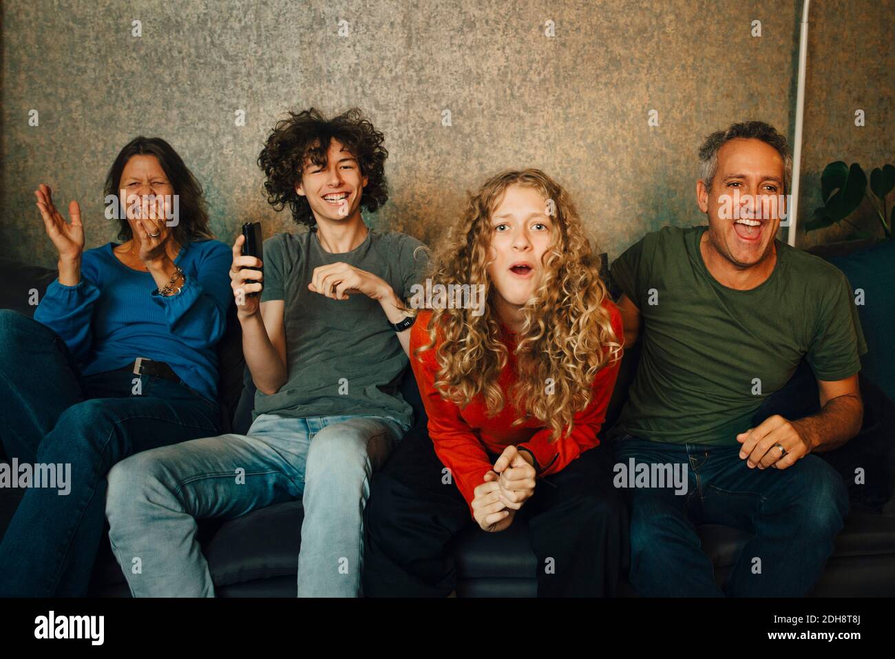 Happy parents and children cheering while watching sports in living ...
