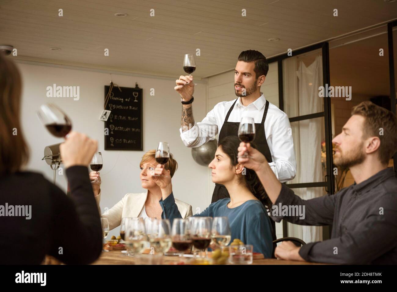 Man standing by people and analyzing wineglass at table Stock Photo - Alamy