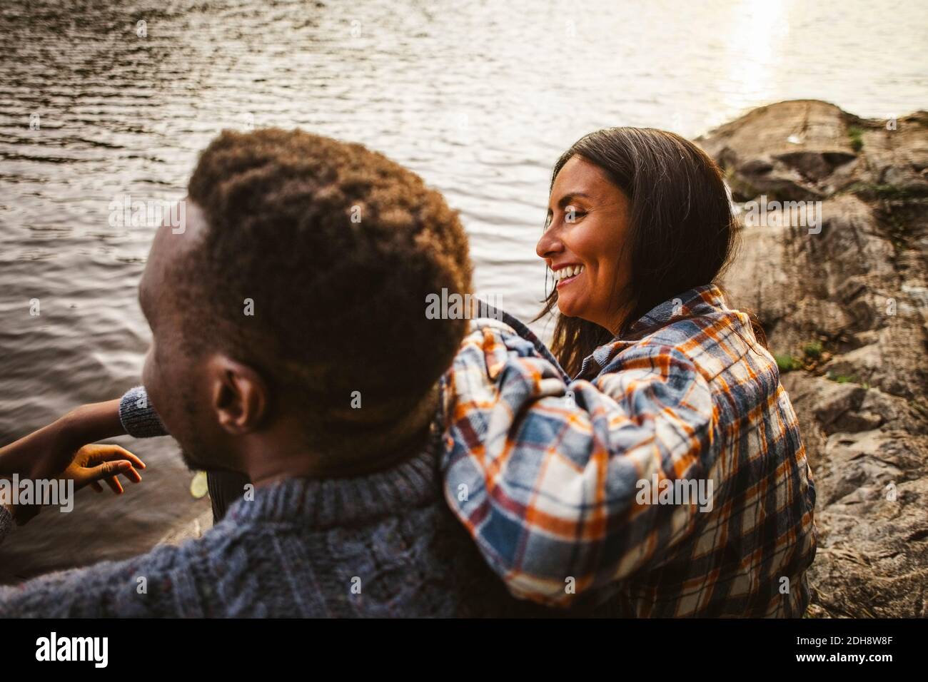 Side view of smiling woman and man sitting by lake in forest Stock ...