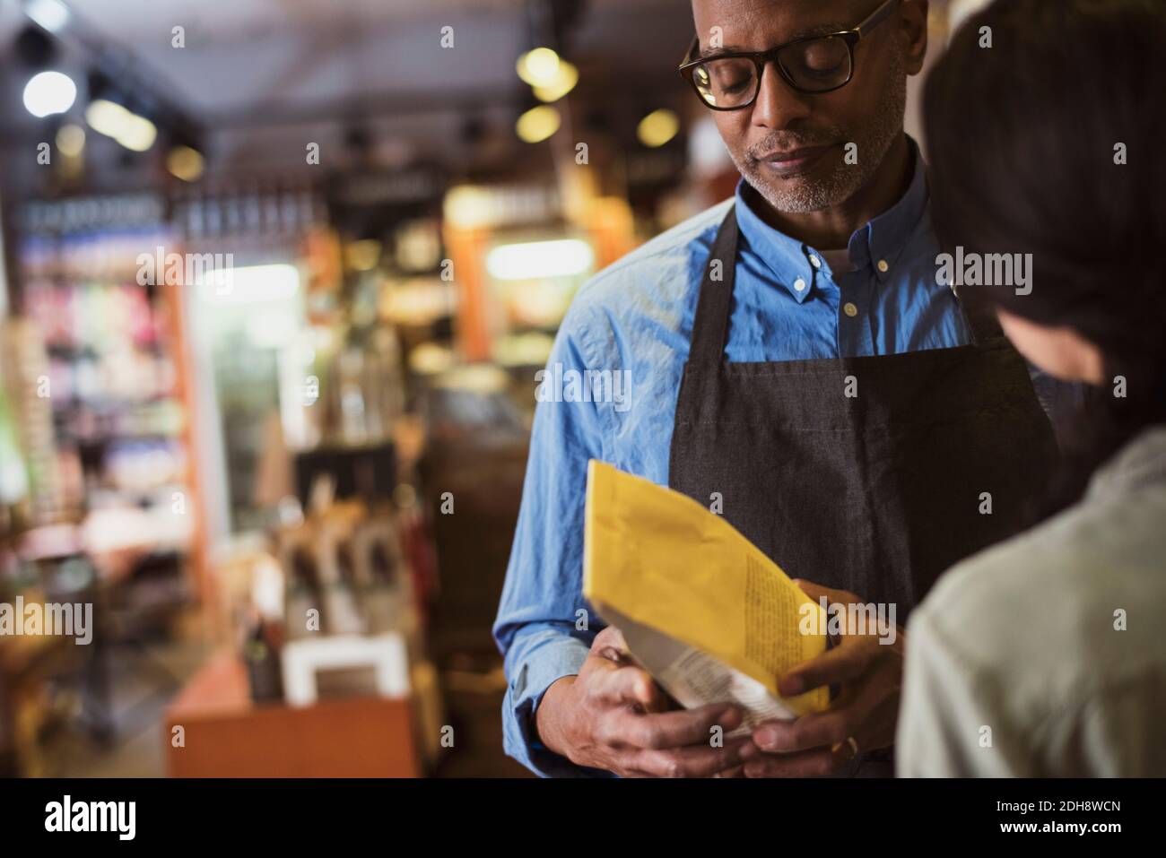Owner reading label on food packet while standing with customer at ...