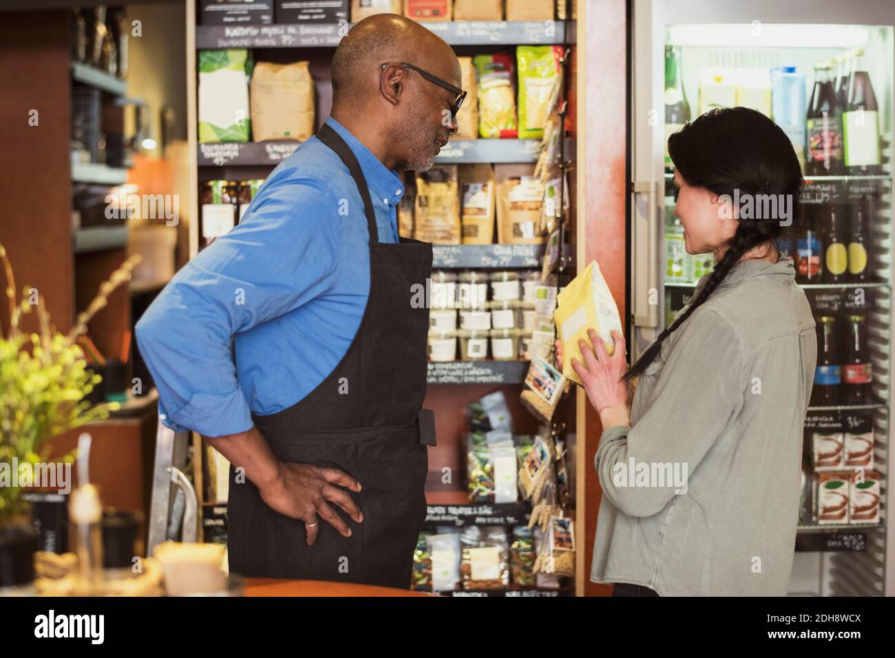Owner looking at female customer reading labels on packets at store ...