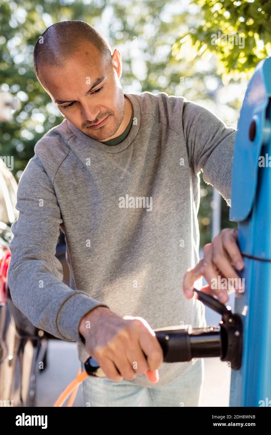 Man plugging cable at electric station Stock Photo - Alamy