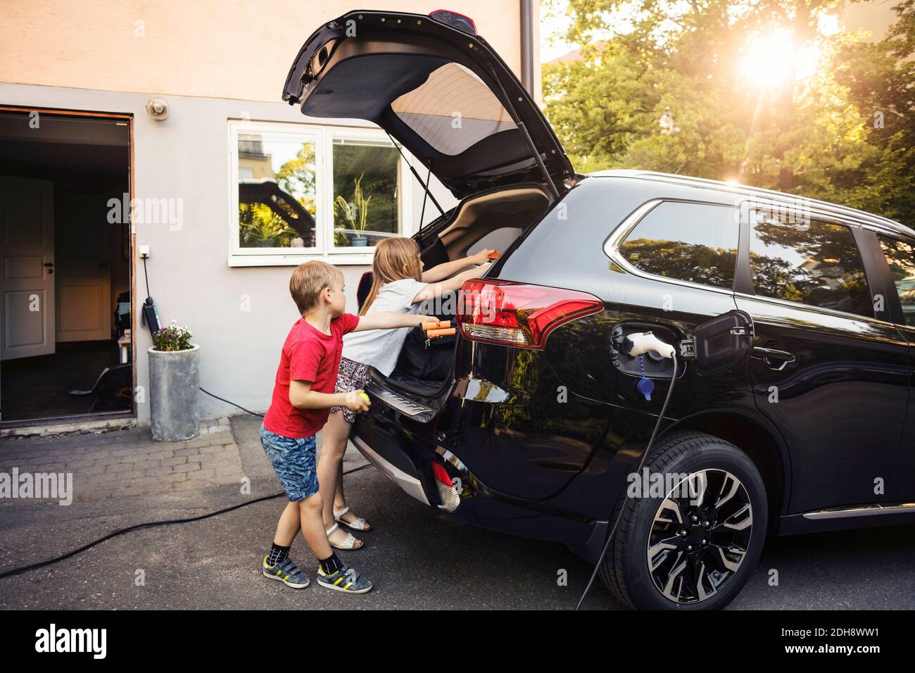 Kids loading black electric car trunk against house in back yard Stock ...