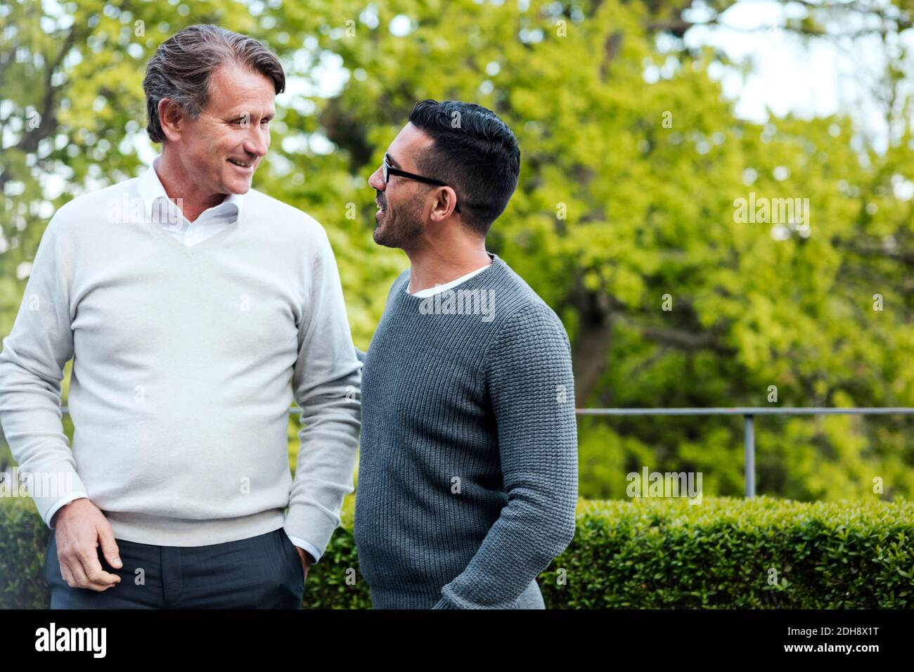 Smiling multi-ethnic friends talking while standing against hedge in ...