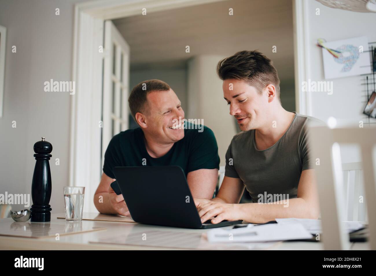 Male talking to smiling partner while using laptop over dining table at ...