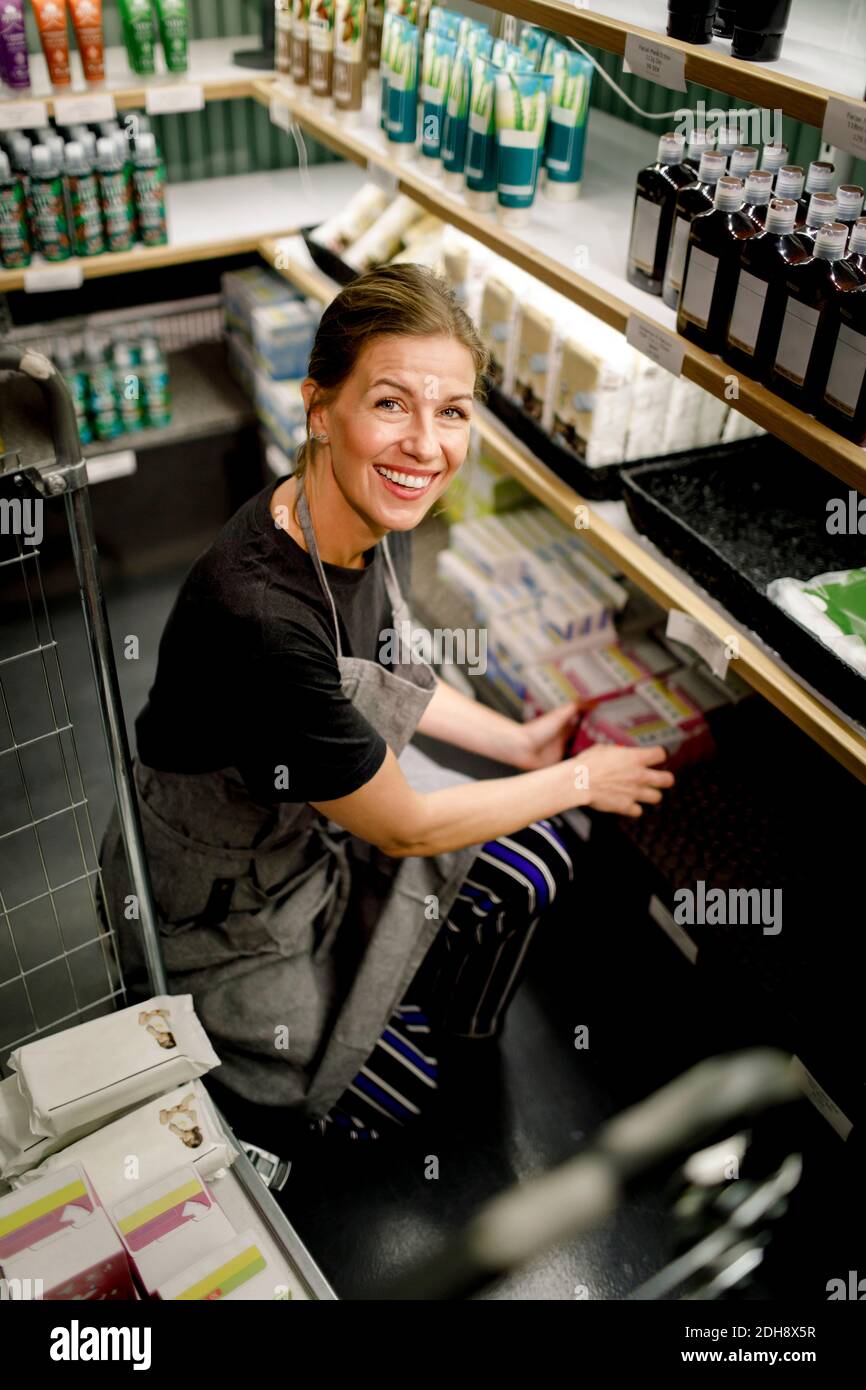 Portrait of smiling saleswoman crouching while working in supermarket ...