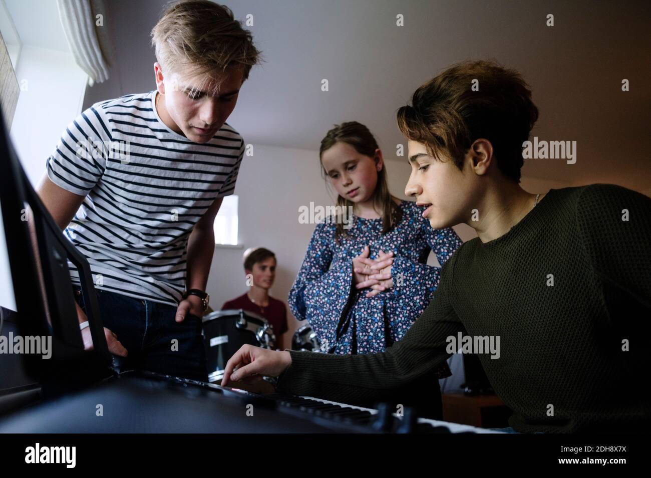 Young friend explaining siblings while playing piano keyboard at home ...
