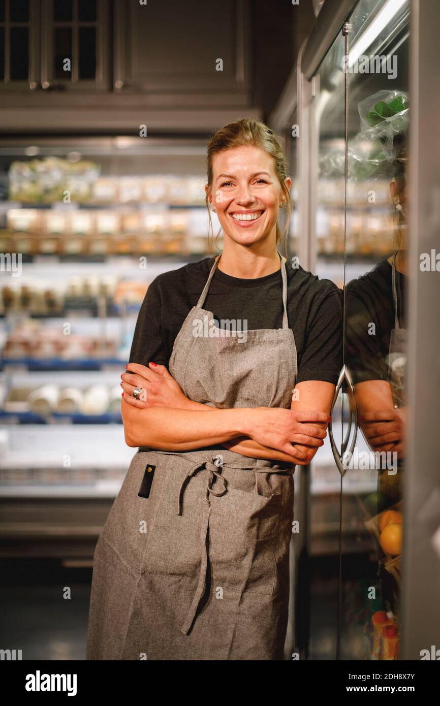 Portrait of smiling saleswoman with arms crossed leaning over ...