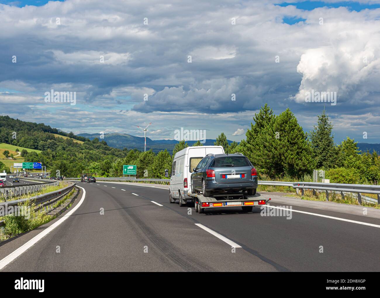 White minibus with tow truck transporter on highway. Car carrier ...