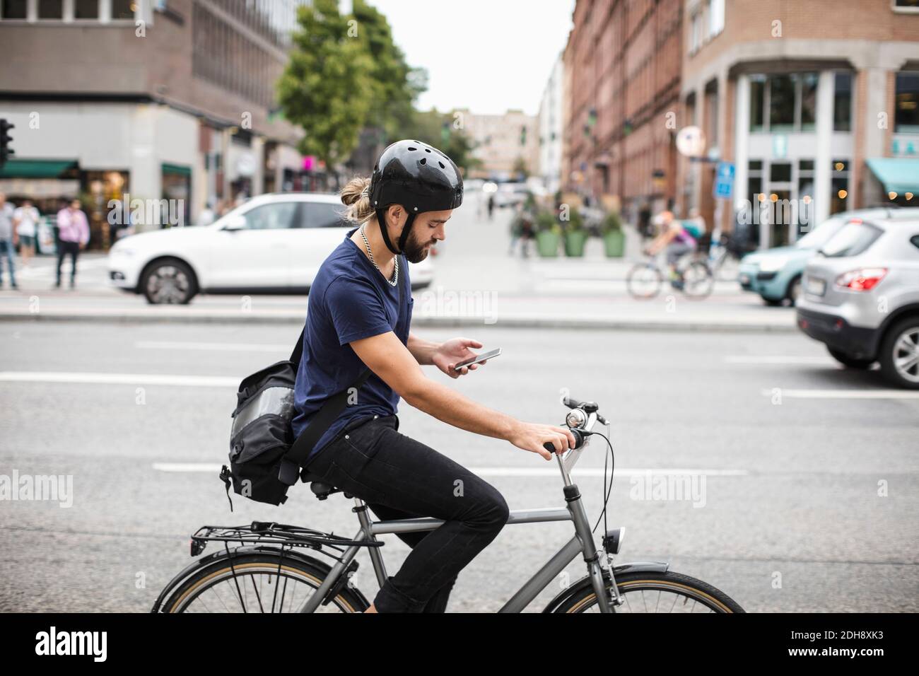 Side view of man using mobile phone while riding bicycle on city street ...