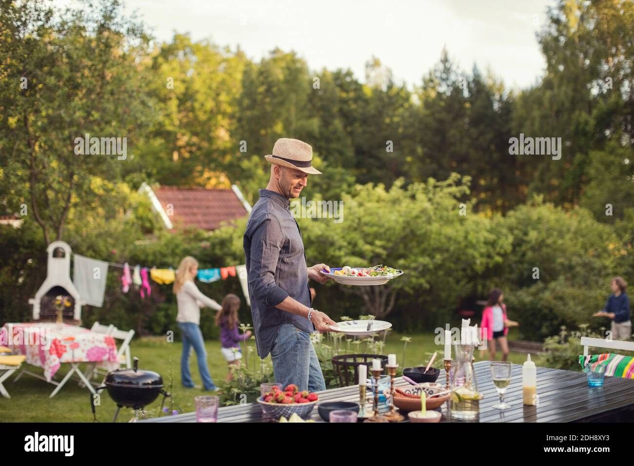 Man carrying plates by dining table in back yard during garden party ...
