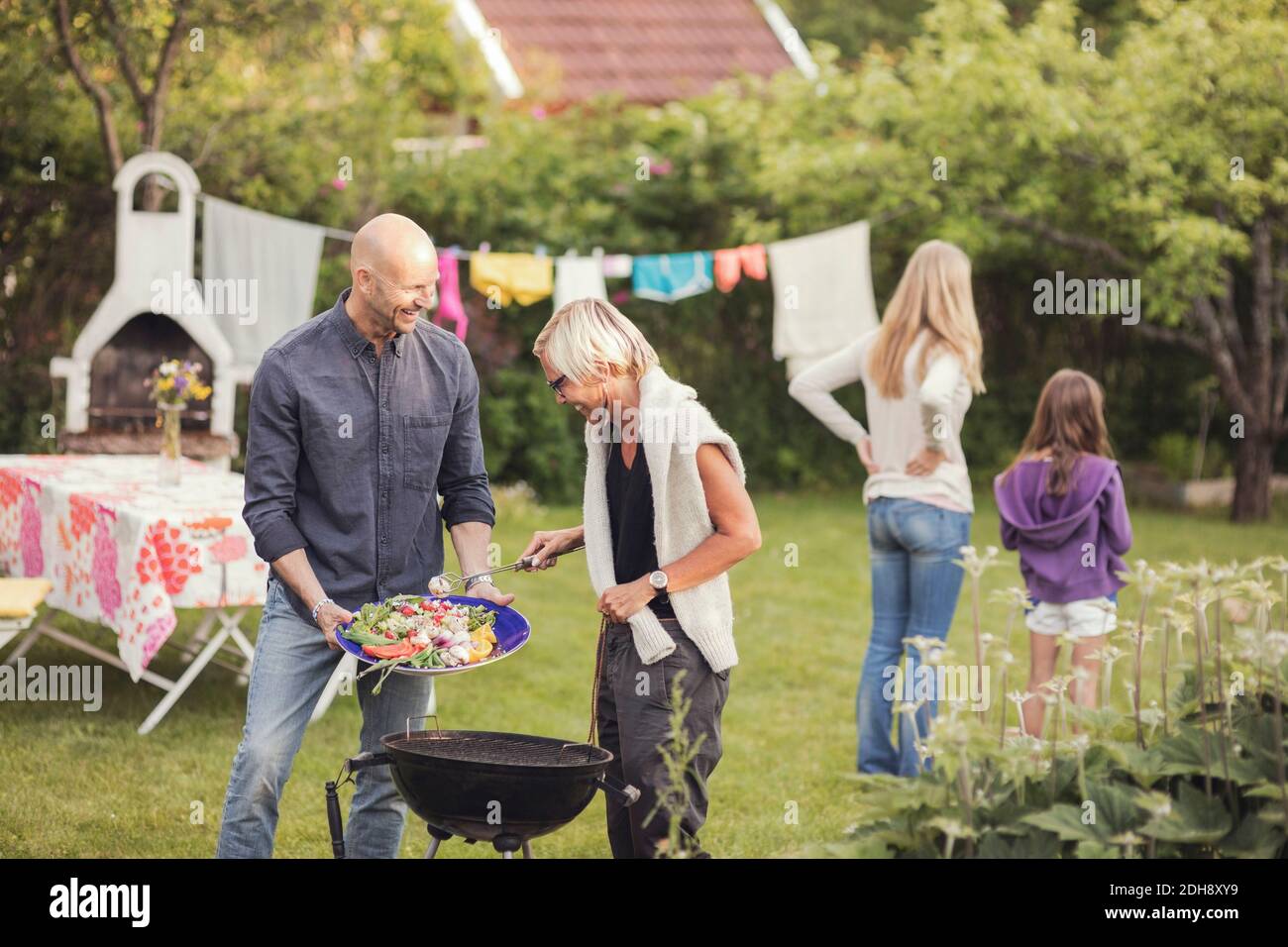 Man and woman cooking vegetables on barbecue grill with girls standing ...