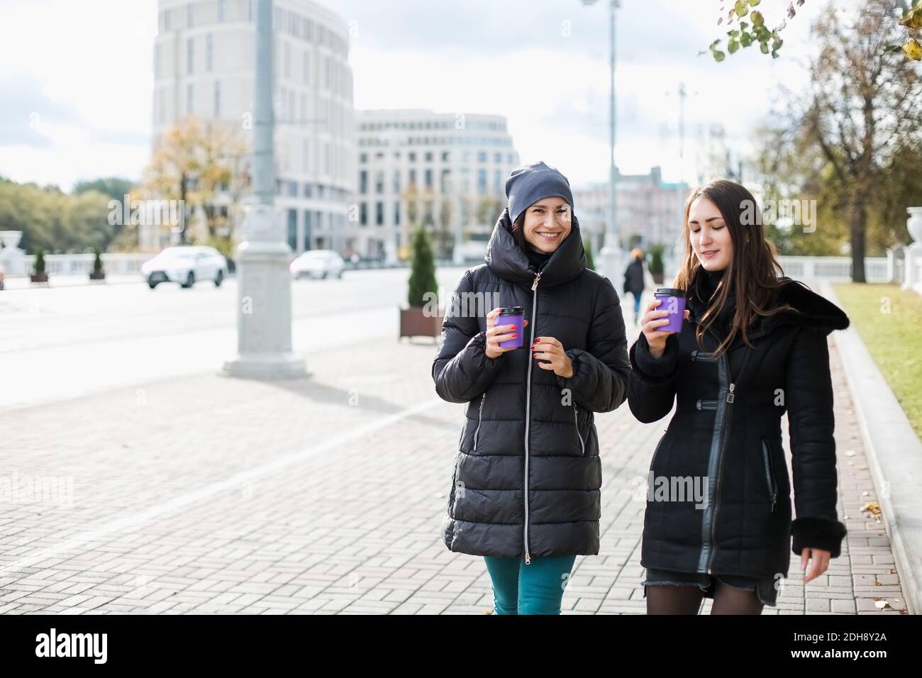 Two girls walk around the city talking, cups in their hands Stock Photo ...