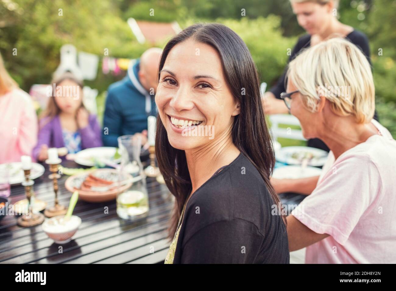 Portrait of happy woman sitting with family and friends at dining table ...