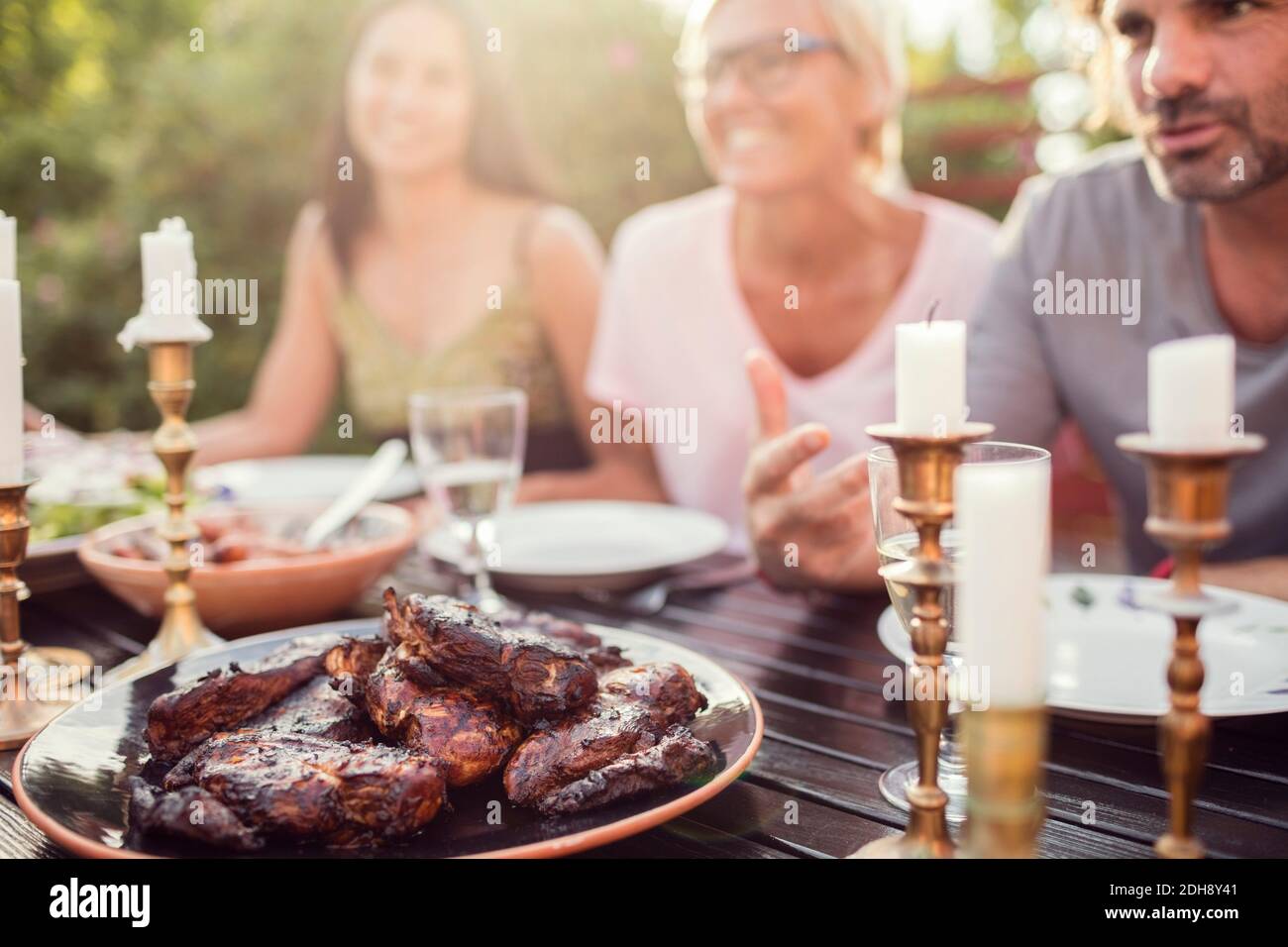 Couple and female friend sitting at dining table during garden party in ...