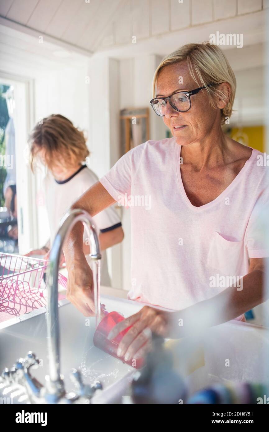 Woman washing utensil with boy standing in kitchen Stock Photo - Alamy