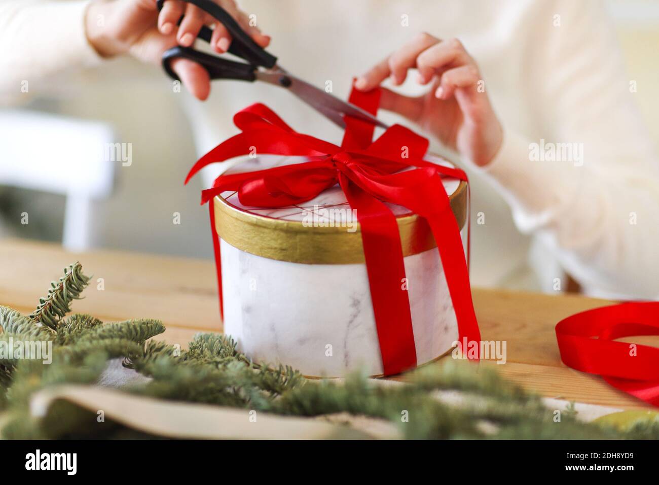 Young girl in white sweater packing round present box tied with bright ...