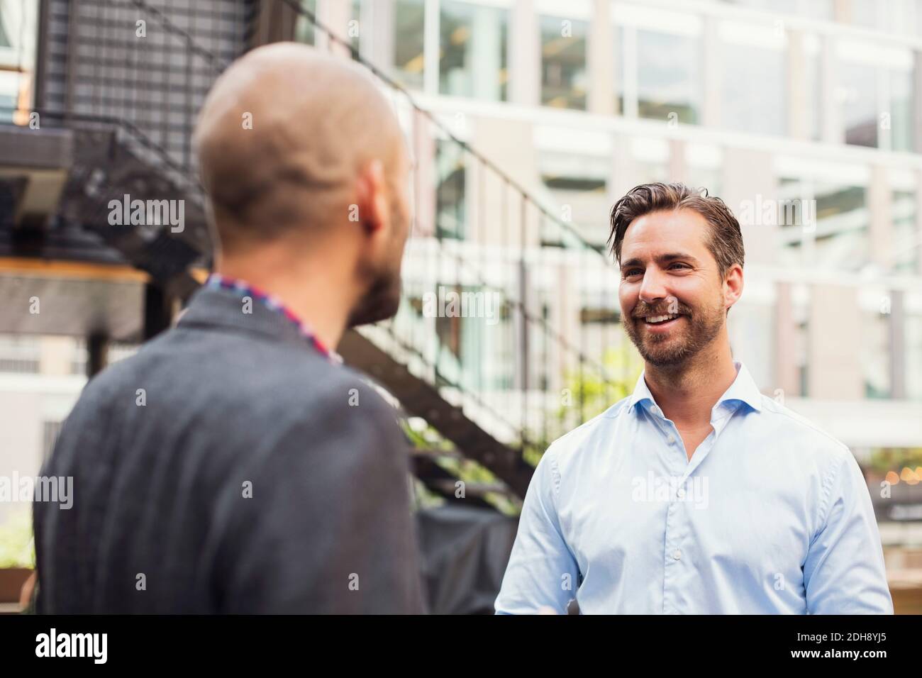 Happy businessman talking to male colleague at office yard Stock Photo ...