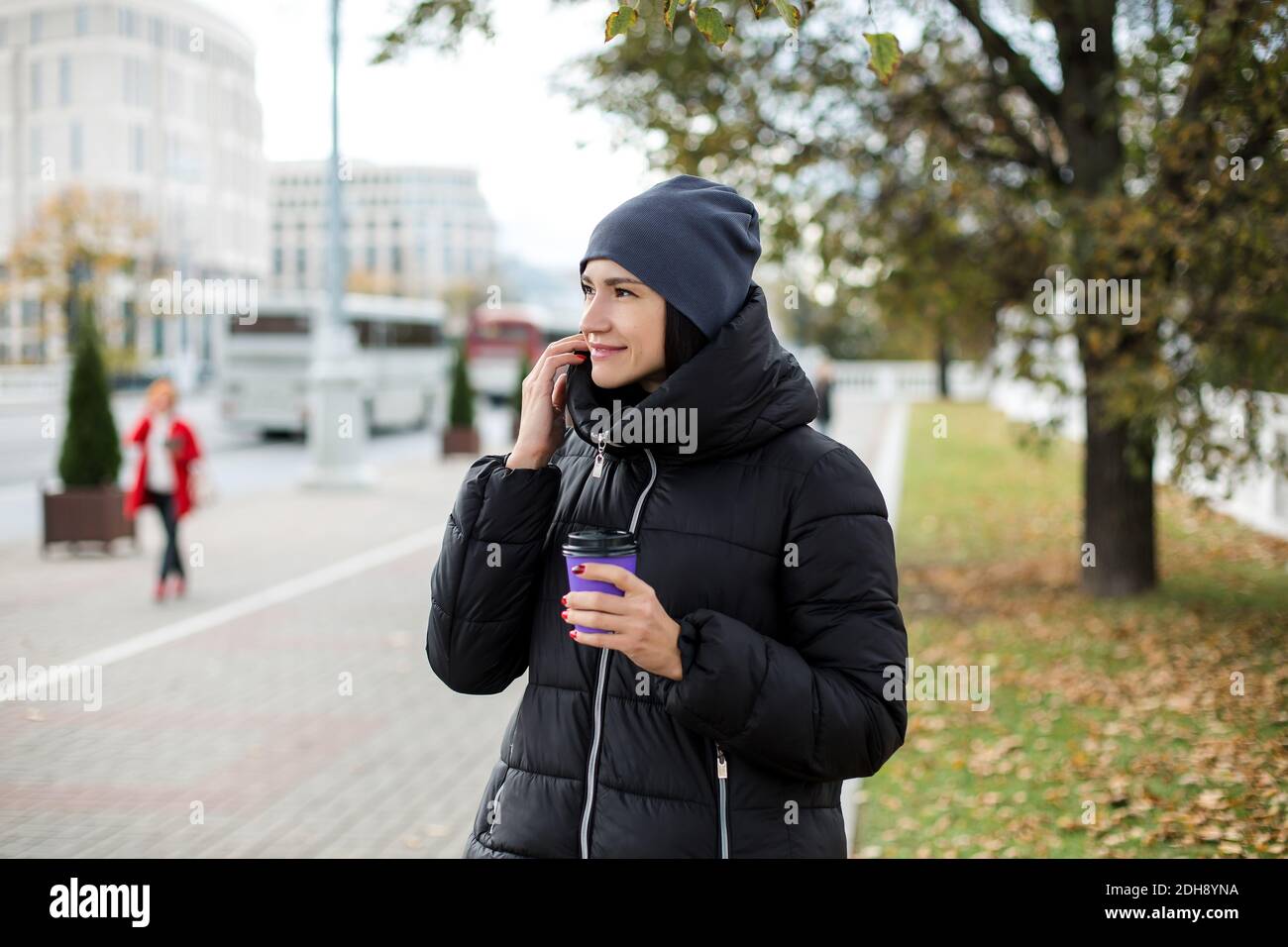 Girl in a jacket and a hat on the street, holding a glass and a phone ...