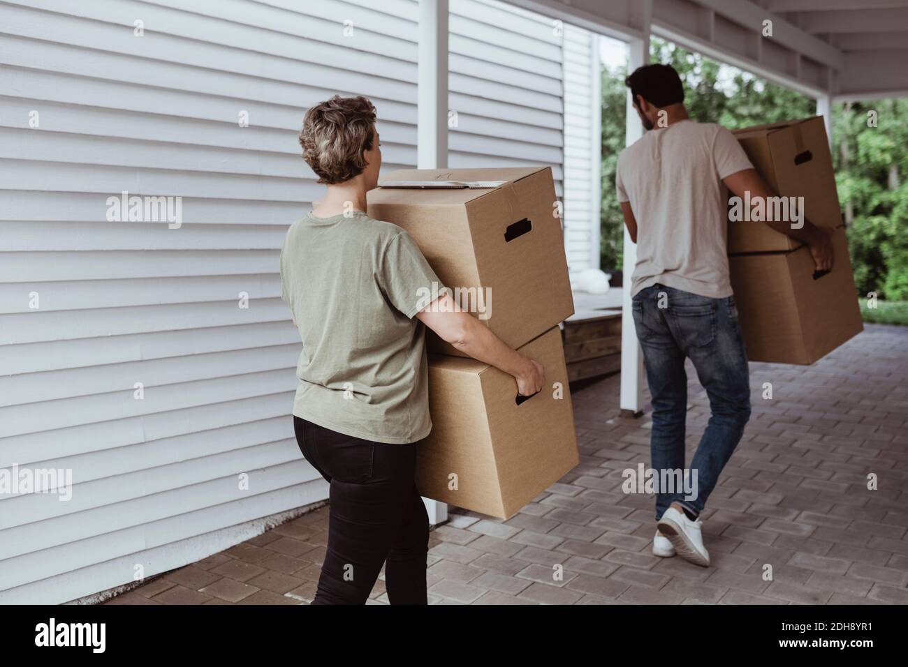 Rear view of male and female carrying cardboard boxes outside house ...