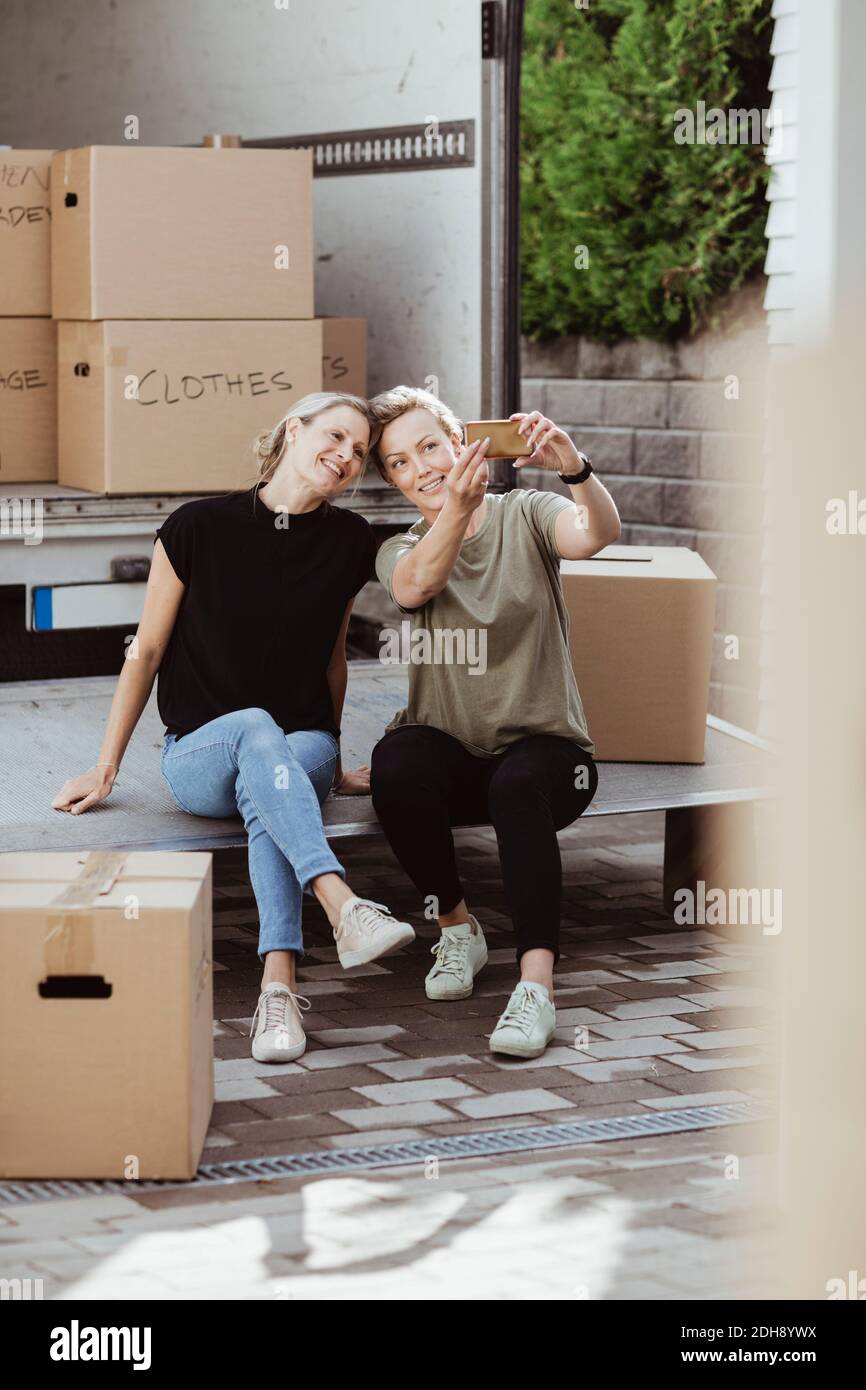 Female friends taking selfie while sitting cardboard boxes during ...
