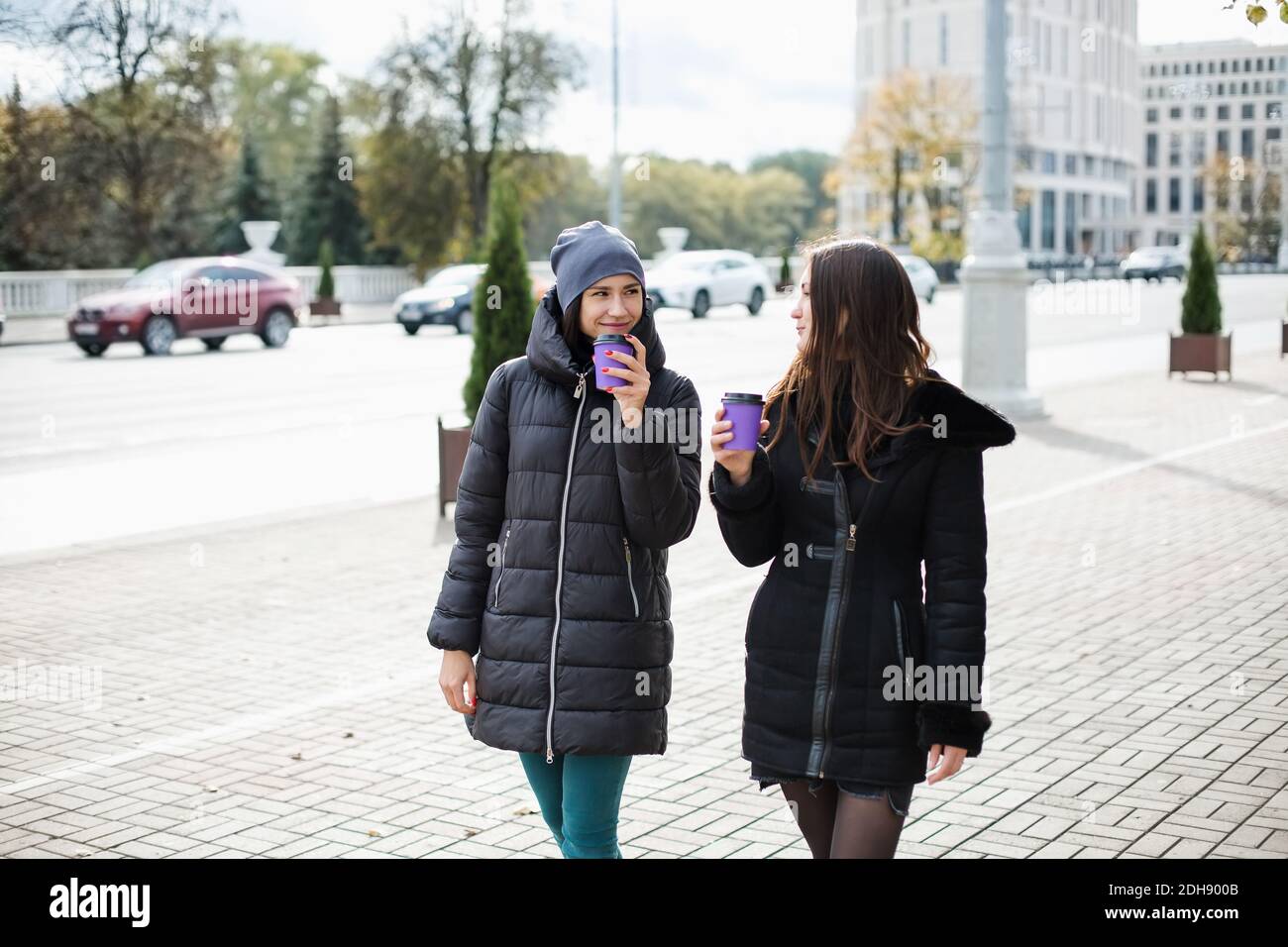 Two girls walk around the city talking, cups in their hands Stock Photo ...