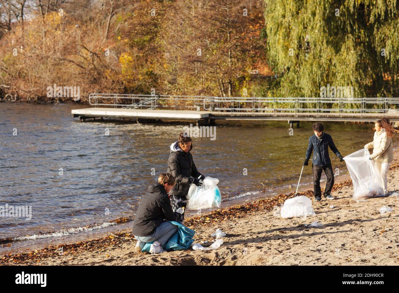 Male and female friends collecting plastic garbage by lake Stock Photo ...