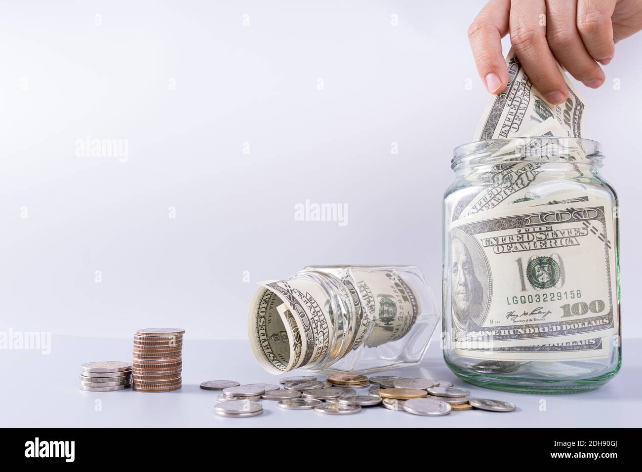 Hand putting money paper into jar with stack coins isolated grey ...