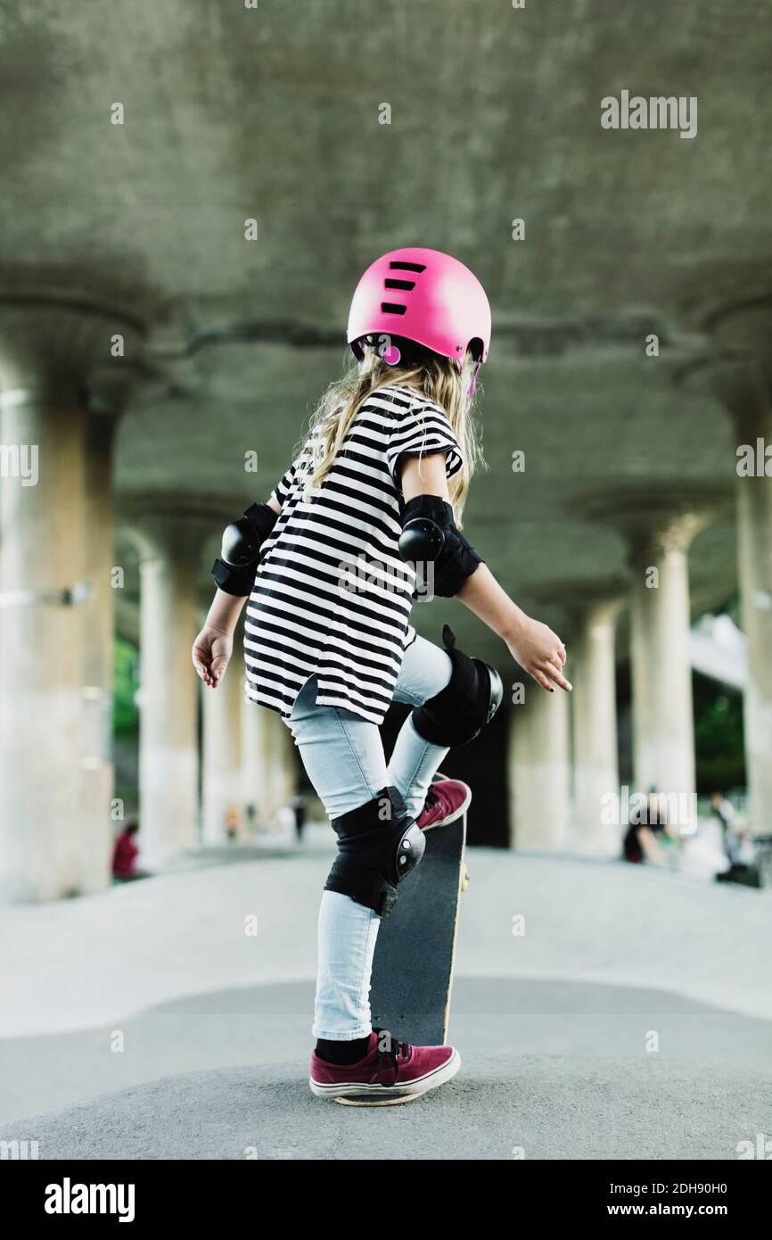 Rear view of girl performing stunt with skateboard at park Stock Photo ...