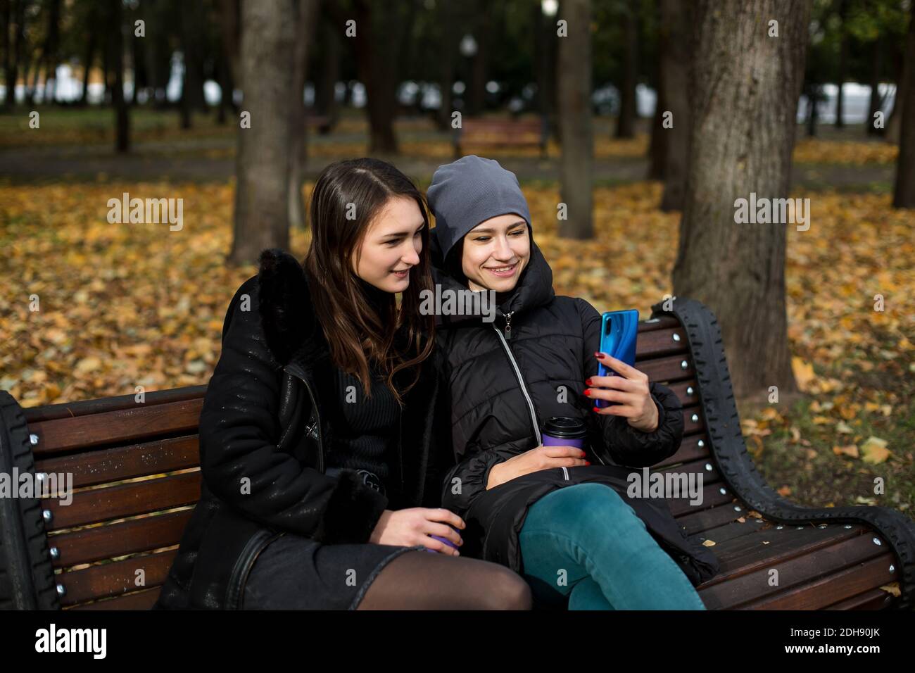 Two girls in the park talk on a bench with a phone and a glass Stock ...