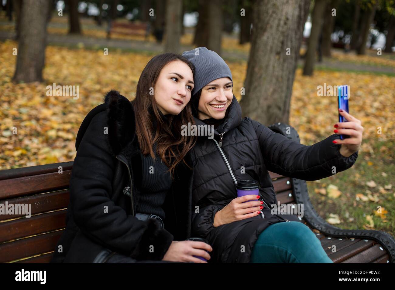 Two girls in the park talk on a bench with a phone and a glass Stock ...