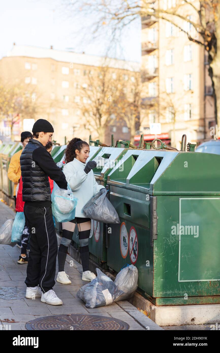 Young male and female environmentalists throwing waste in garbage can ...