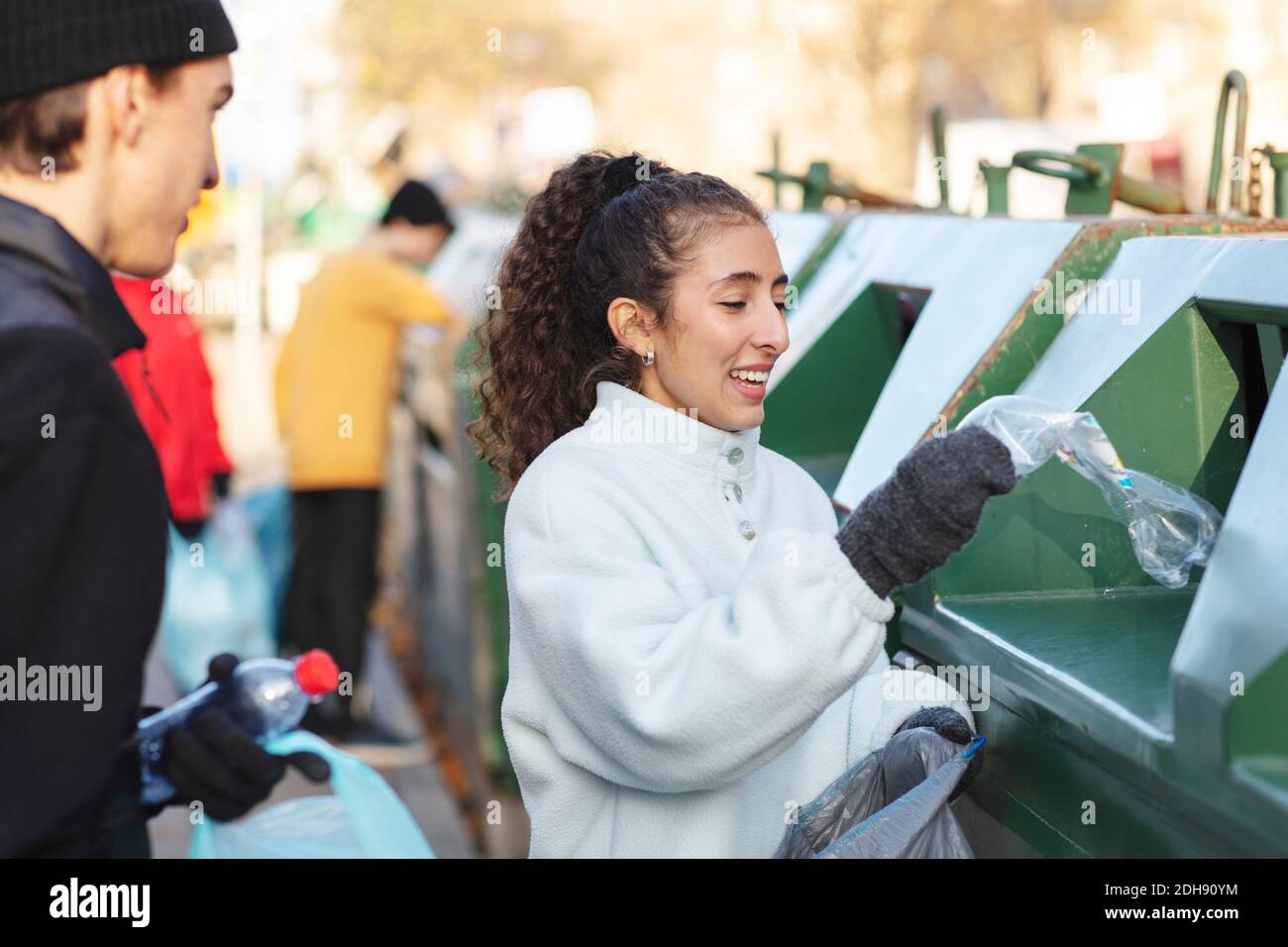 Smiling female environmentalist with friend throwing waste in garbage ...