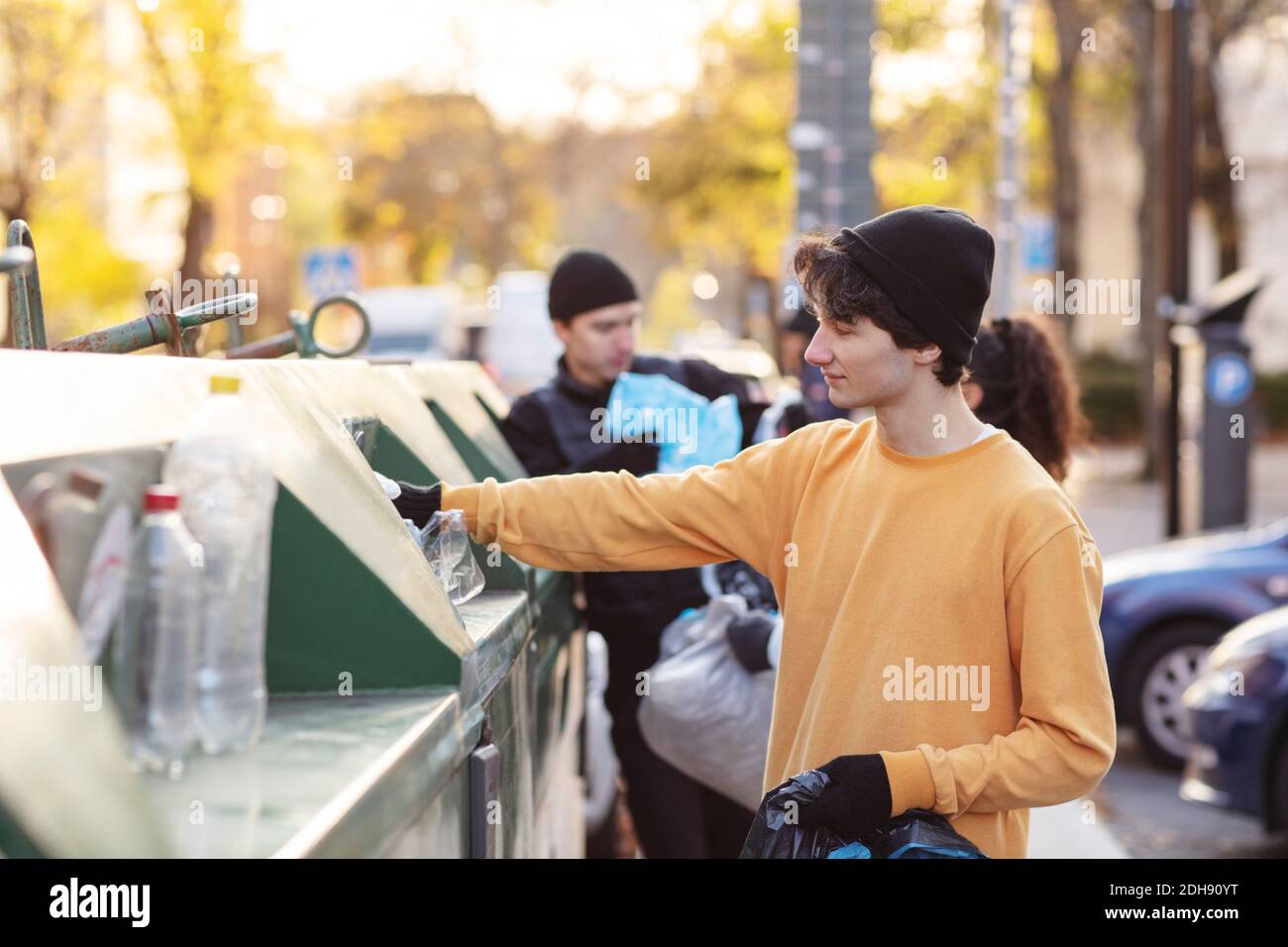 Smiling male environmentalist throwing plastic waste in garbage can ...