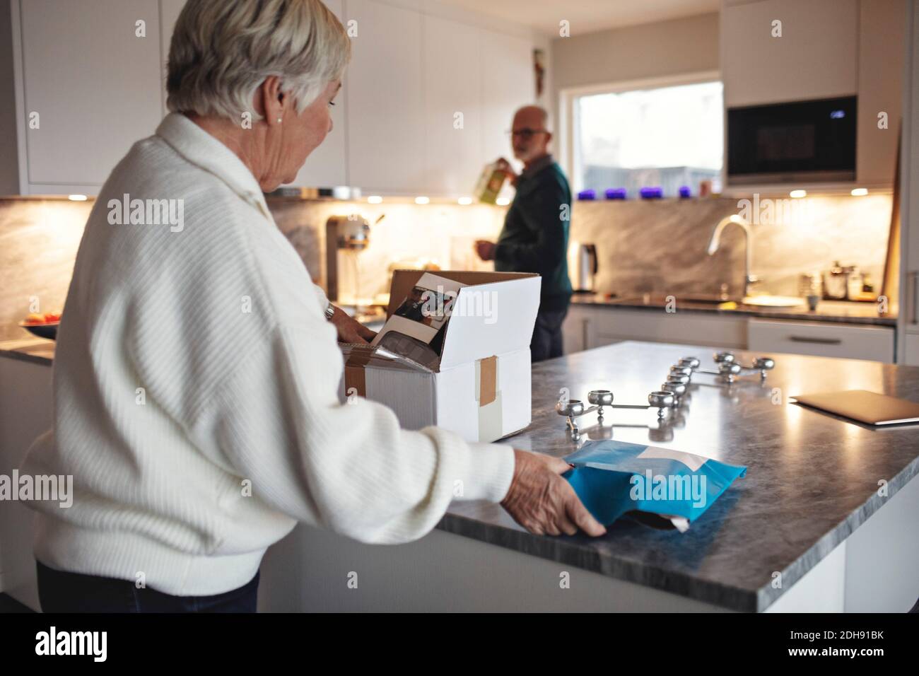 Side view of senior woman unpacking box over kitchen island Stock Photo ...