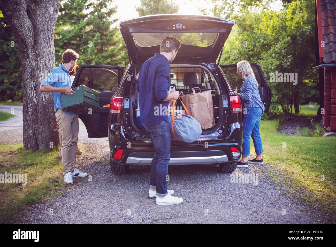 Friends loading luggage into car while standing on road Stock Photo - Alamy