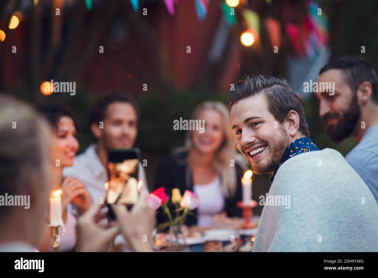 Woman photographing man while sitting with friends at garden party ...